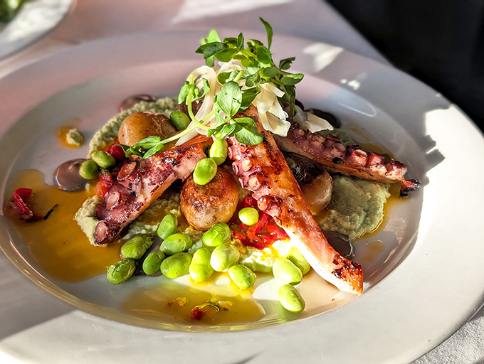 Grilled octopus transforms from sea creature to culinary masterpiece, artfully plated with vibrant vegetables and Mediterranean flair.