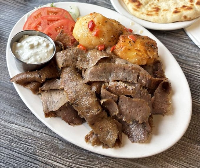 This gyros platter showcases tender sliced meat alongside roasted potatoes that glisten like Mediterranean sunset gems.