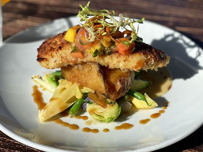 Macadamia-crusted halibut perched atop vegetables like a culinary high-wire act &ndash; proof that sometimes the most delicious things are also the most precarious.