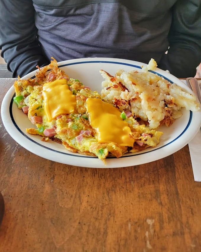 When breakfast meets art: an omelet stuffed with ham and veggies, crowned with melted cheese, alongside hash browns that could make a potato proud.