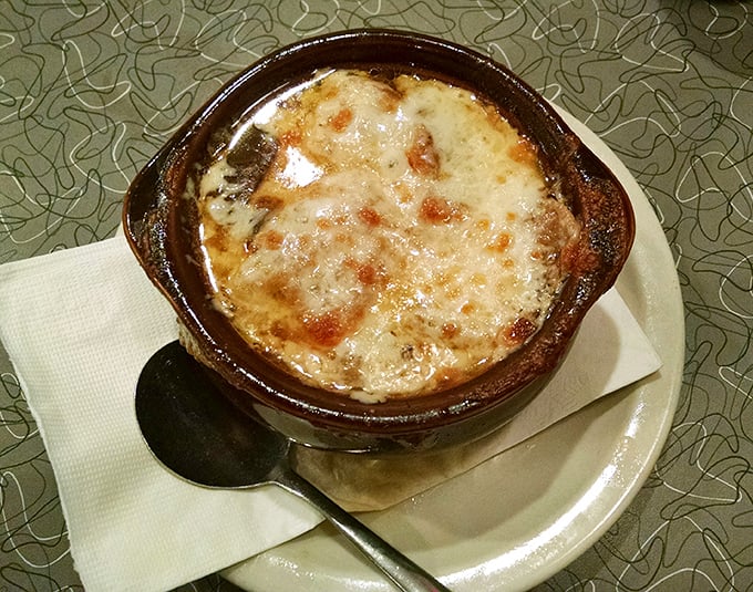 Steam rises from this onion soup like aromatic poetry, promising warmth that reaches straight to your heart.