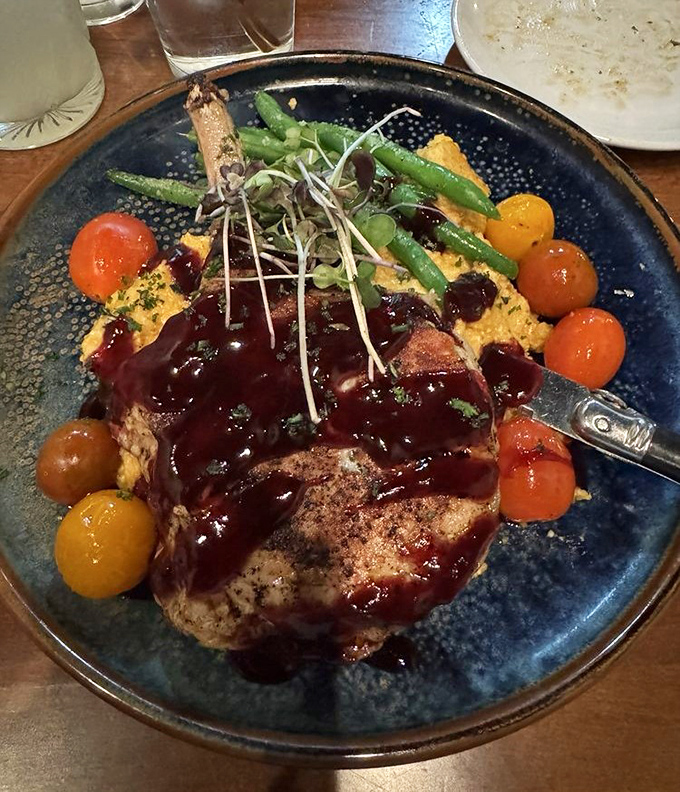 A pork chop that's dressed for success with a glossy sauce, colorful tomatoes, and a bed of creamy polenta. This isn't dinner&mdash;it's edible theater on a blue plate.