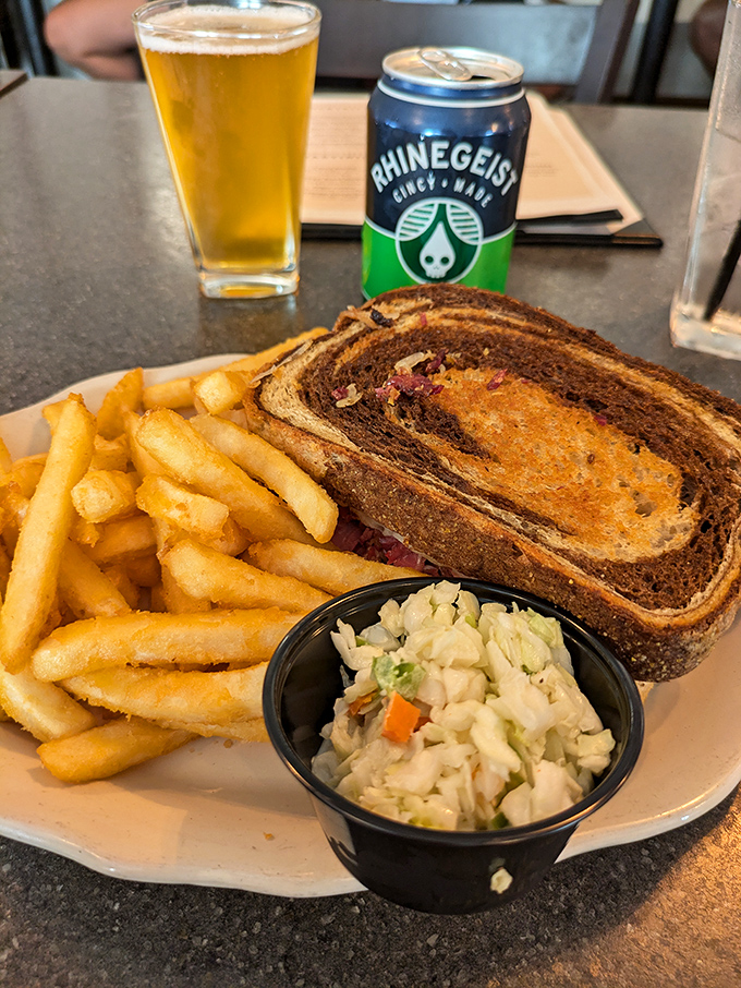 That's not just a sandwich &ndash; it's a marbled rye masterpiece with what looks like proper Reuben fillings, accompanied by the holy trinity of fries, slaw, and beer.