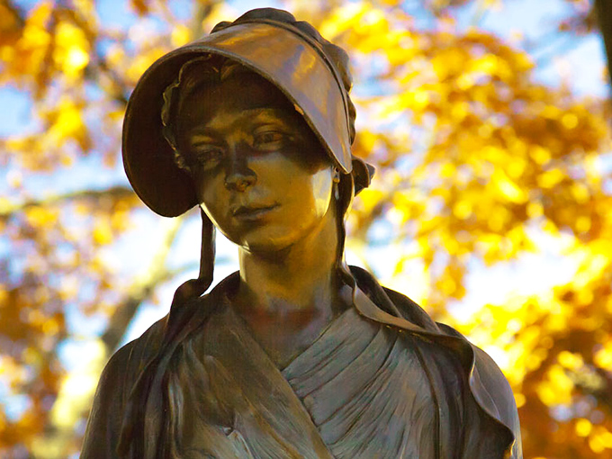 This bronze figure stands sentinel through changing seasons, her contemplative gaze unchanged whether surrounded by summer greenery or autumn's golden display.