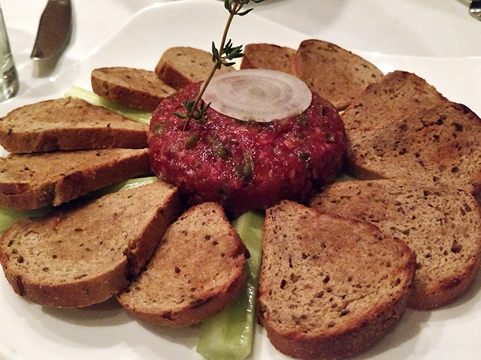 Steak tartare arranged like an edible sunflower. Raw beef never looked so civilized, surrounded by its bread petal entourage.