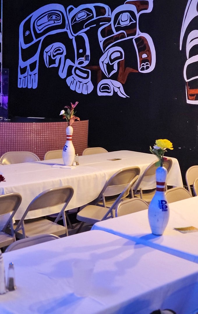 Bowling pin centerpieces and tribal art create an unexpected visual feast in the event space, where folding chairs somehow look perfectly at home.