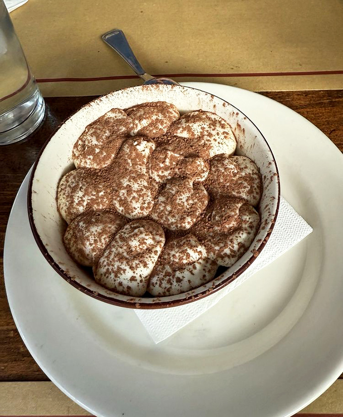 Tiramisu that looks like a cloud formation of coffee-soaked dreams. The cocoa dusting is generous because life's too short for stingy desserts.