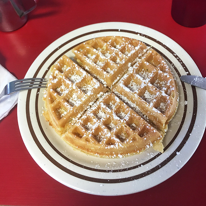 This waffle wears powdered sugar like a crown, ruling over breakfast plates with sweet, fluffy authority everywhere.