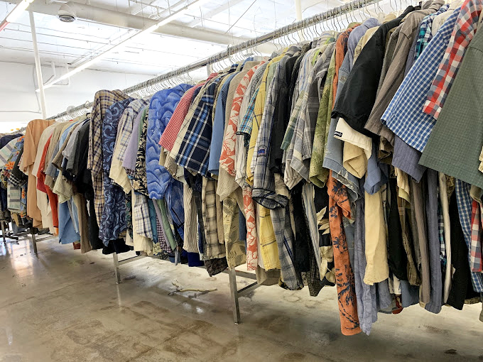 The men's shirt section offers more patterns than a kaleidoscope factory, each hanger holding someone's past and your potential future.