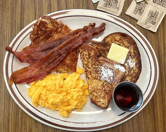 The holy trinity of breakfast: perfectly scrambled eggs, crispy bacon, and French toast dusted with powdered sugar. Morning salvation on a plate.