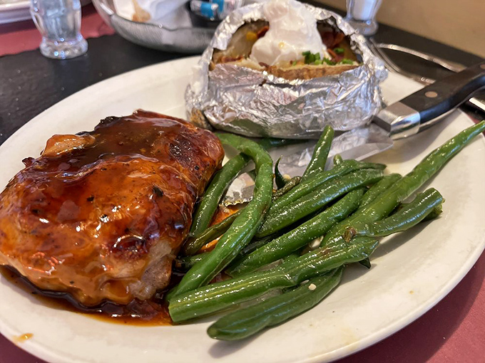 Barbecue-glazed chicken alongside fresh green beans and a foil-wrapped potato—proof that not everything delicious needs to moo first.