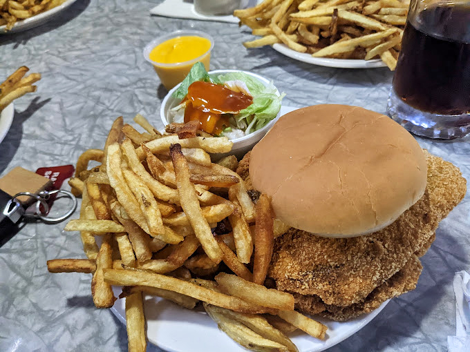 The pork tenderloin sandwich with golden-brown perfection extending well beyond its bun&mdash;a Midwest classic that demands a two-handed commitment.