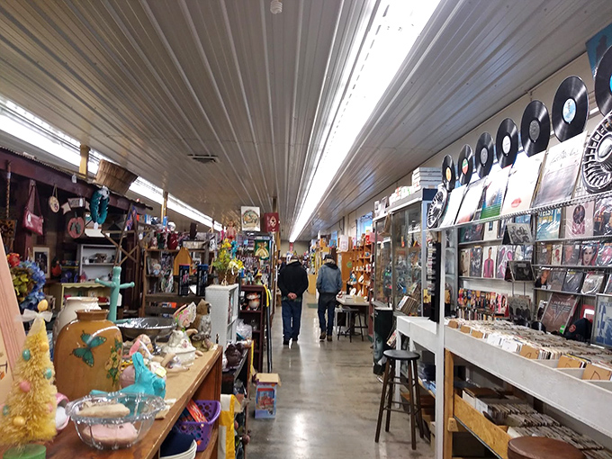 Inside a vintage marketplace with rows of permanent booths filled with collectibles and vinyl records, two visitors stroll through the aisles.