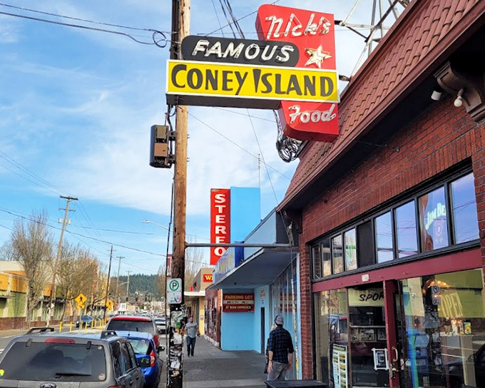 Classic brick storefront with that iconic sign glowing above. The sidewalk bench invites you to savor your coney dog while watching the world go by.