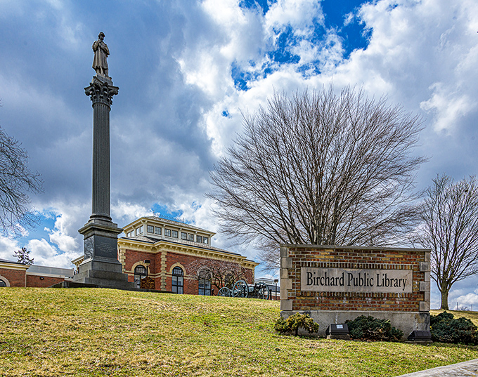Birchard Public Library stands proudly beside its monument, a temple of knowledge where community and history converge under dramatic Ohio skies.