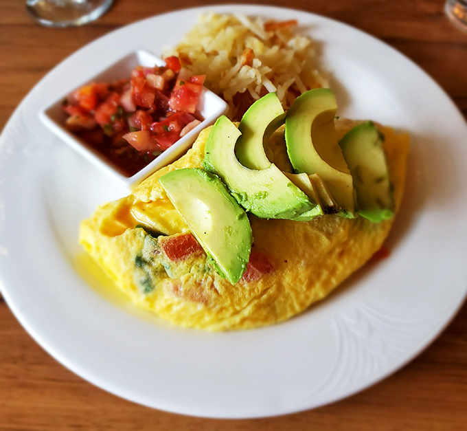 Breakfast nirvana: a fluffy omelet adorned with avocado slices, with pico de gallo and hash browns standing by as worthy supporting actors.