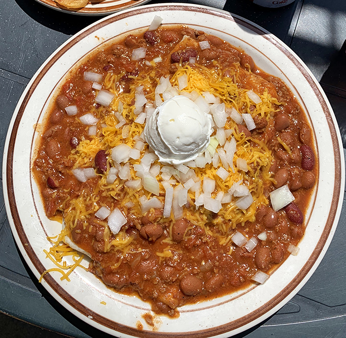 A bowl of homemade chili crowned with cheese, onions, and a dollop of sour cream. Spoon-worthy artwork that warms the soul.
