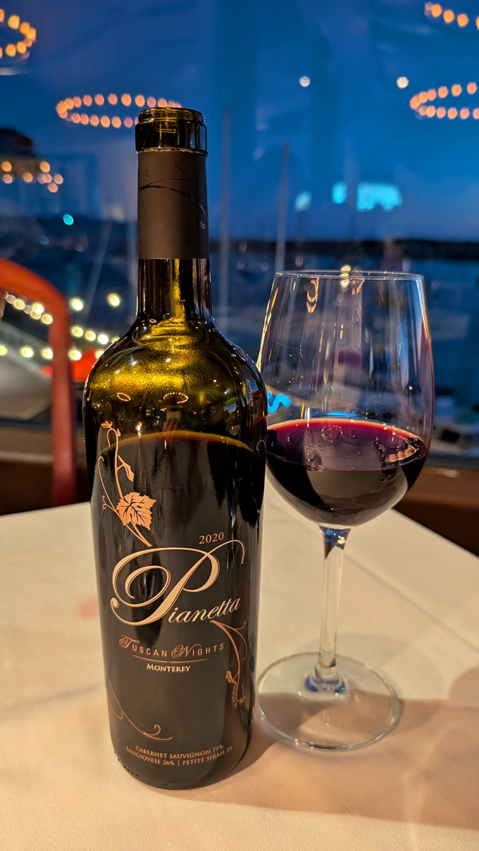 A glass of local red wine with the bay twinkling in the background&mdash;nature's perfect pairing for your seafood feast.