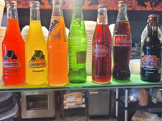 A rainbow of bottled sodas stands at attention, offering sweet relief from the savory smoke parade happening on your plate.