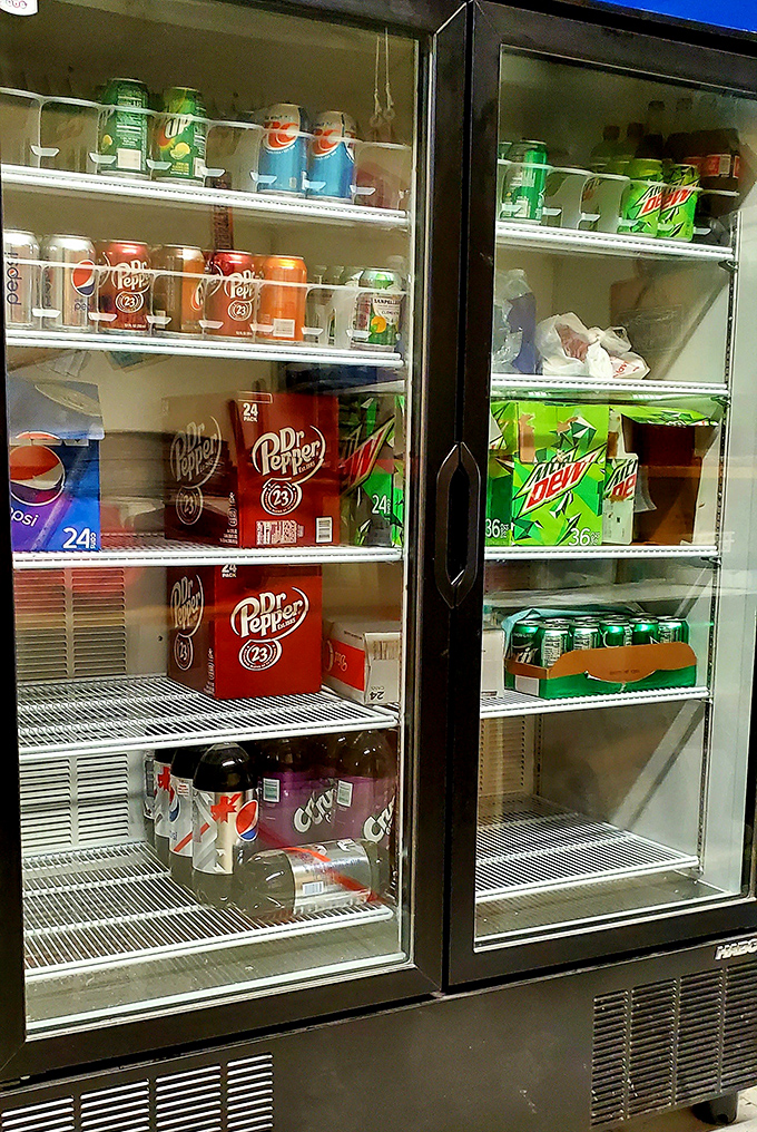 The beverage cooler stands ready like a refreshment arsenal. Nothing fancy, just the cold drinks you actually want with your pizza.