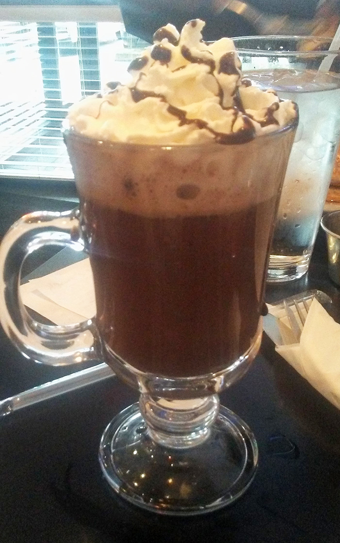 Hot chocolate that understands its assignment&mdash;topped with a cloud of whipped cream and chocolate drizzle in a glass tall enough to impress even your sweet tooth.