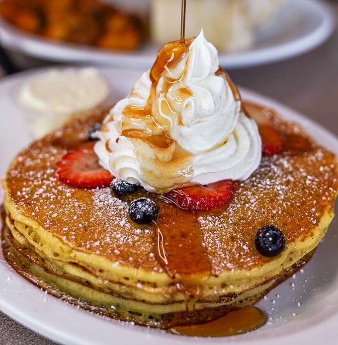 Pancakes topped with berries, whipped cream, and maple syrup cascading down like a sweet waterfall. Breakfast or dessert? Yes.
