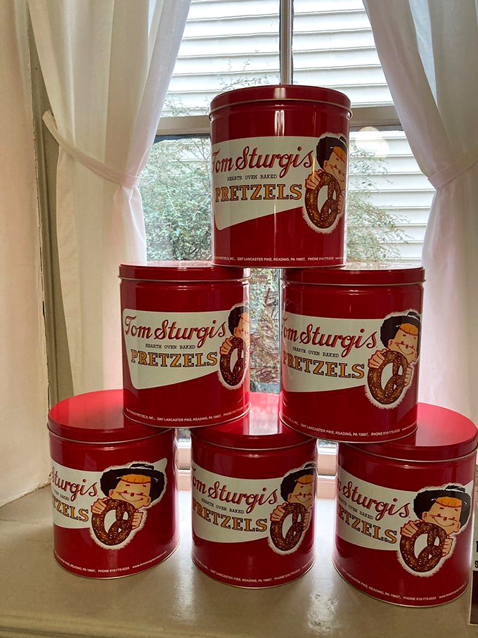 Vintage red pretzel tins stacked by the window&mdash;collectibles that actually contain something worth collecting besides dust and regret.