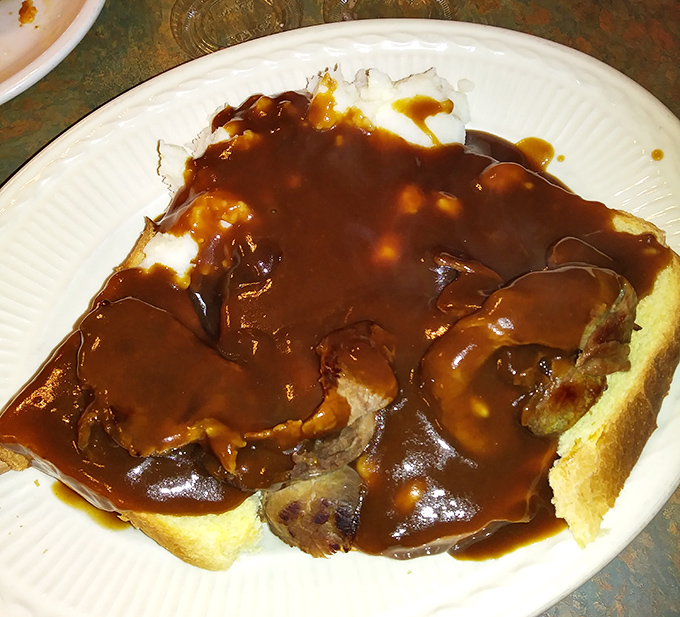 Open-faced roast beef sandwich swimming in rich gravy. Not Instagram food—this is the real deal that grandparents ordered before social media existed.