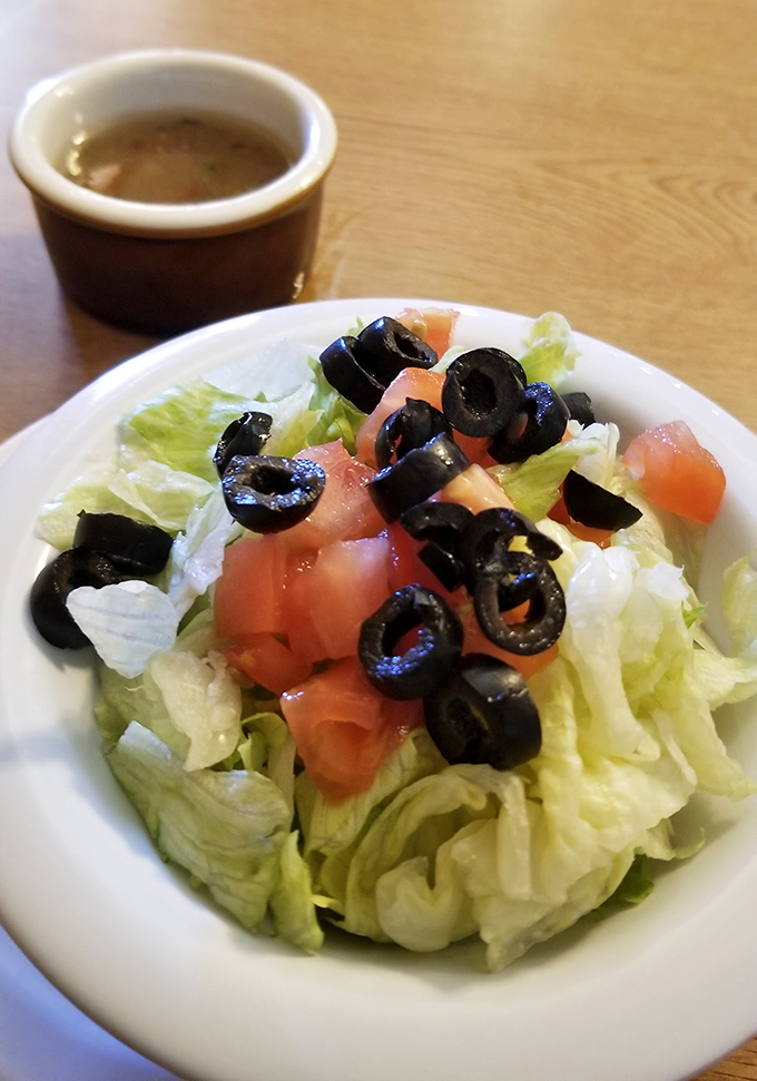 A side salad that knows its role&mdash;crisp lettuce, fresh tomatoes, and olives standing by to provide the illusion of virtue before the main event arrives.