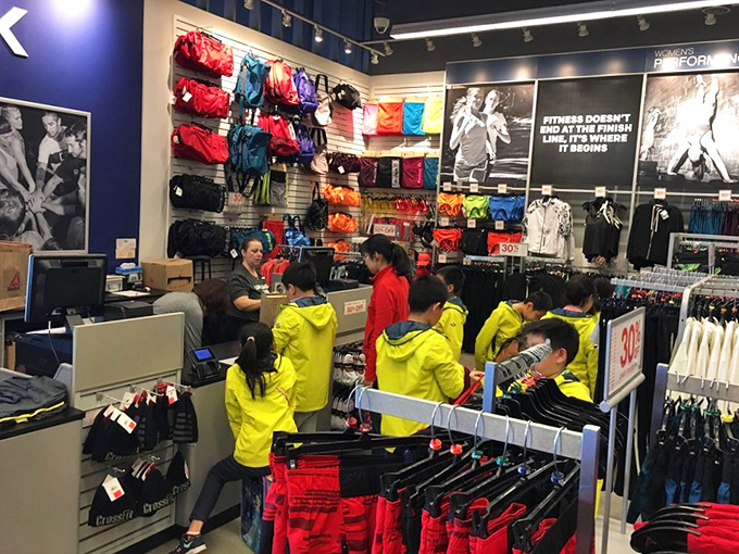 Young shoppers in matching yellow jackets swarm the Reebok store like a school of tropical fish, hunting for deals with youthful enthusiasm.