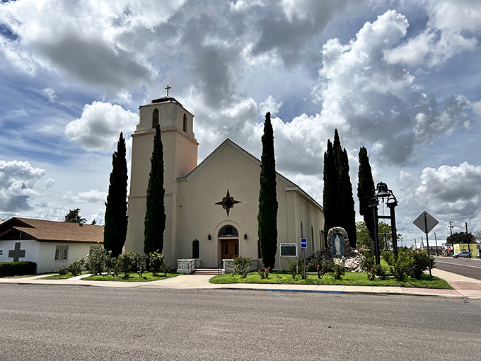 St. Mary's Catholic Church stands serene against dramatic Texas clouds, its white walls and cypress trees creating a Mediterranean vibe in the Chihuahuan Desert.