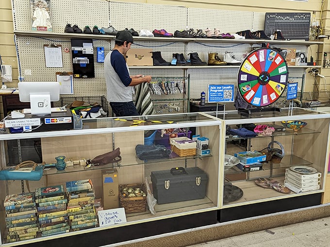 Behind the glass counter, a staff member carefully arranges treasures while the colorful prize wheel promises an extra dash of thrift store luck.