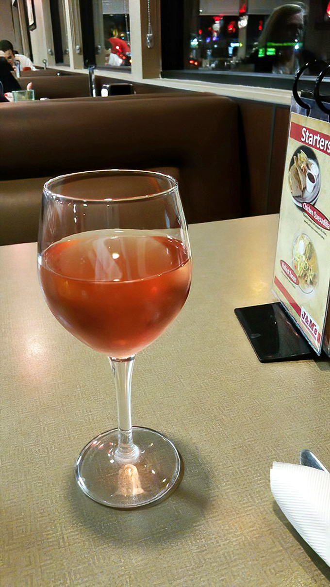 A glass of ros&eacute; sits elegantly beside the table menu, proving that unpretentious dining doesn't mean sacrificing life's little refinements. Wine not?