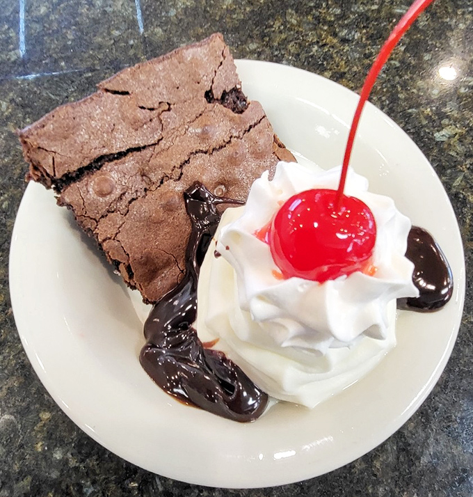 A brownie sundae that understands the importance of balance: warm, fudgy brownie meets cool whipped cream, with that cherry standing guard like a tiny red sentinel.