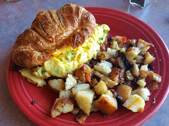 Breakfast architecture at its finest: a buttery croissant cradling fluffy eggs alongside home fries that could make a potato farmer weep with pride.