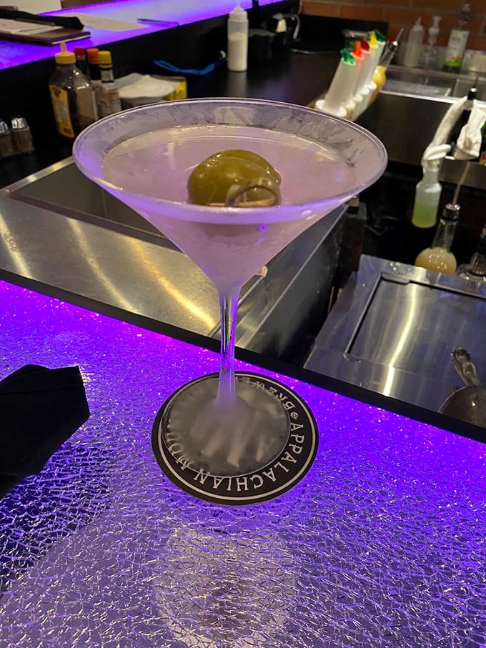 A martini that sparkles under purple light like liquid jewelry. That olive isn't just garnish&mdash;it's the period at the end of a perfect day.