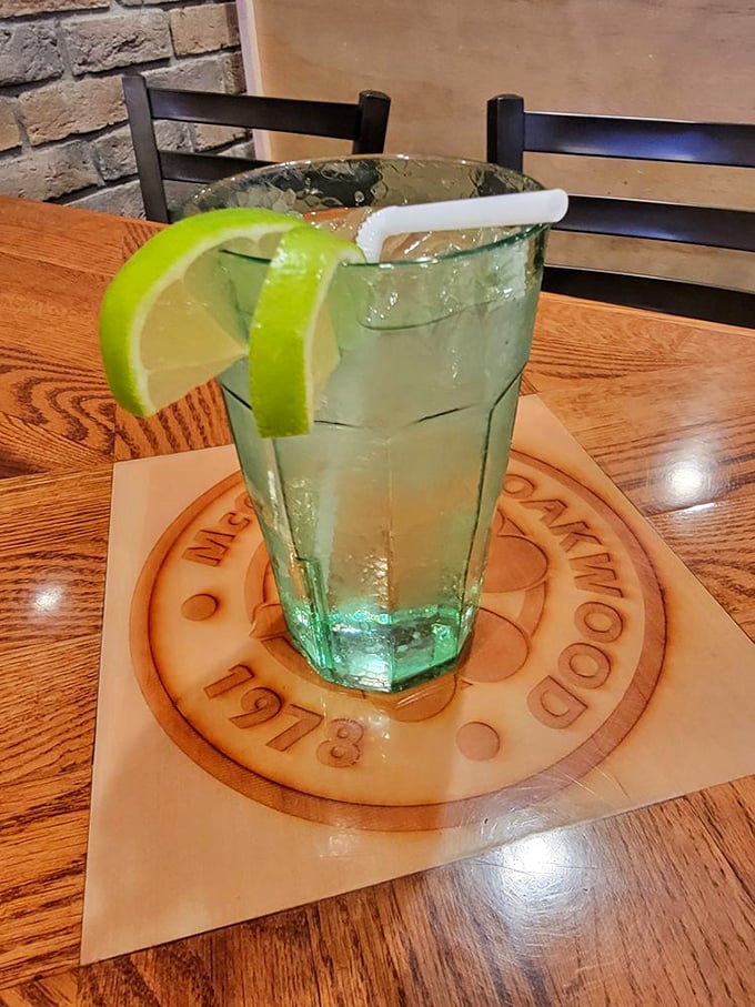 A refreshing drink garnished with lime wedges sits atop a custom coaster. The perfect companion while waiting for sandwich nirvana.