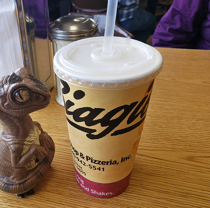 The milkshake cup that promises brain freeze and happiness in equal measure, with a dinosaur friend standing guard.