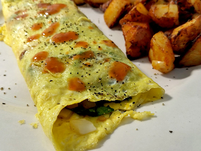 An omelet so perfectly folded it could teach origami classes, dotted with hot sauce freckles that promise a gentle wake-up call.