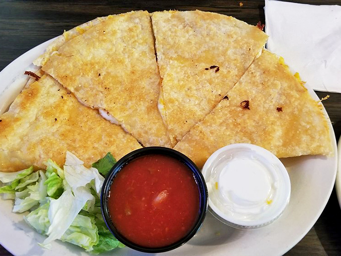 The quesadilla arrives with that perfect golden crisp, accompanied by the holy trinity of toppings&mdash;salsa, sour cream, and shredded lettuce.