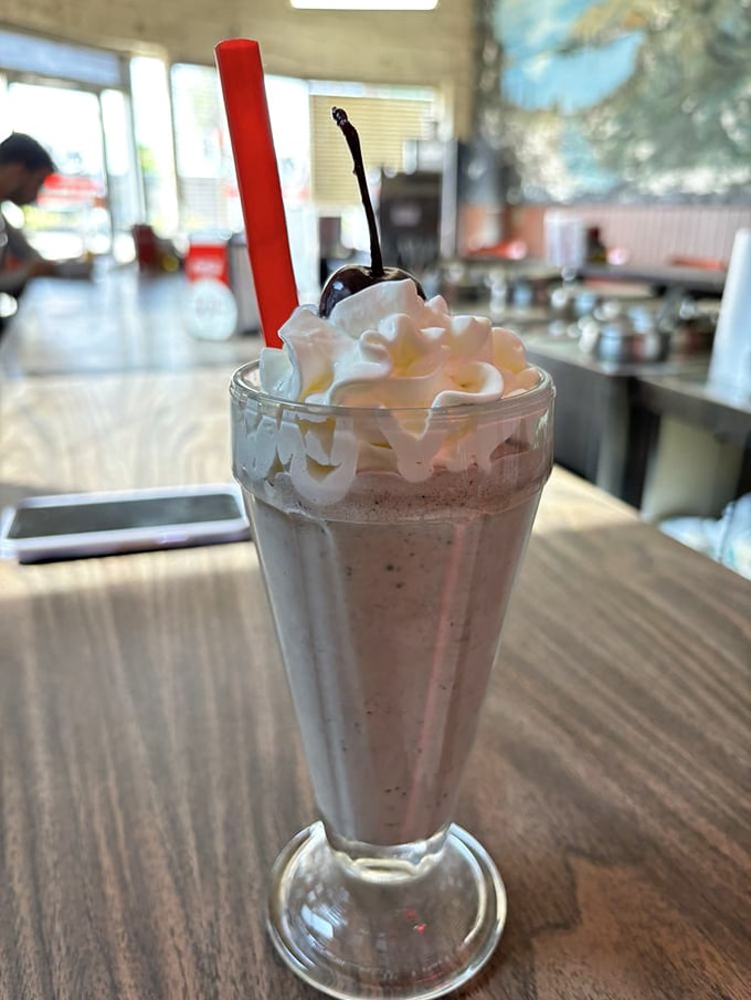The milkshake arrives like a dessert from simpler times&mdash;whipped cream mountain, cherry on top, and that red straw promising sweet relief from the chili heat.