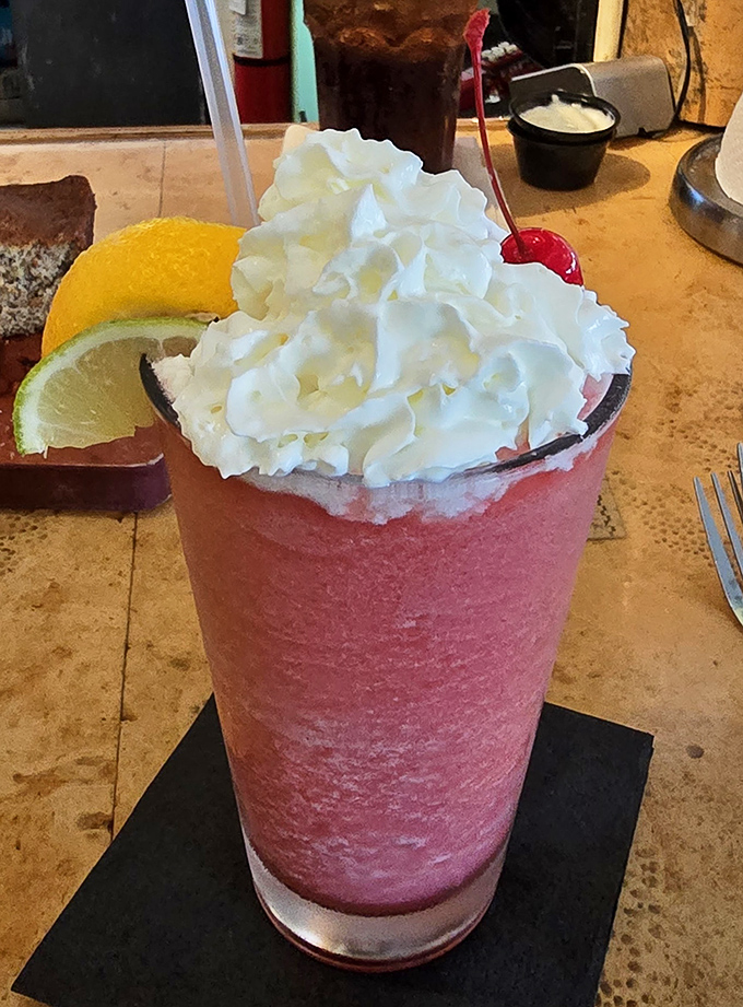 The strawberry shake arrives like a pink tower of nostalgia, topped with enough whipped cream to make your inner child high-five your adult self.