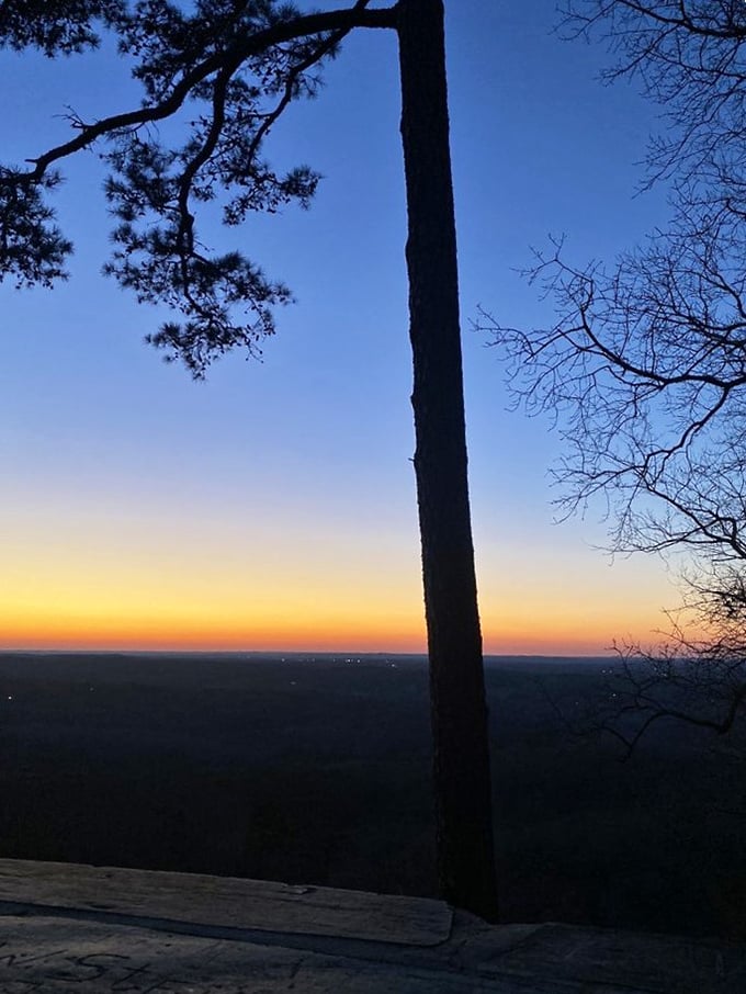 Day's end magic hour at the summit. As the sun sets, distant city lights begin to twinkle while the foreground fades to silhouette.
