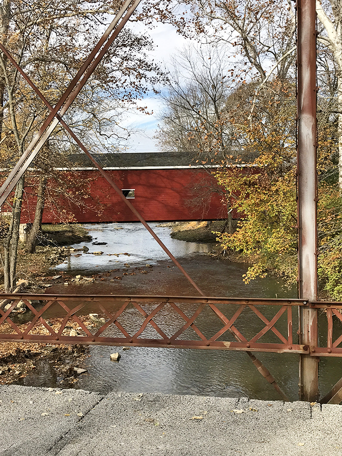 Fall foliage frames the bridge in nature's perfect complementary colors&mdash;the red structure pops against autumn's golden hues like a painting come alive.