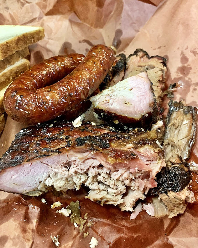 A barbecue still life worthy of the Louvre. The curve of that sausage link alongside the tender brisket creates a composition that speaks to your stomach, not your brain.
