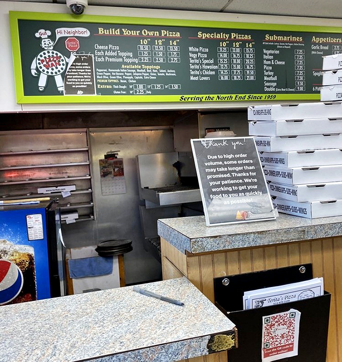 Behind this counter, pizza dreams become reality. The sign politely acknowledges high volume, but really means "good things come to those who wait."