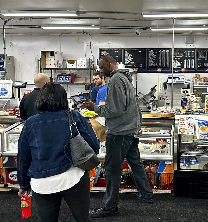 The universal language of sandwich anticipation brings people together at the counter, united in the pursuit of lunch perfection.