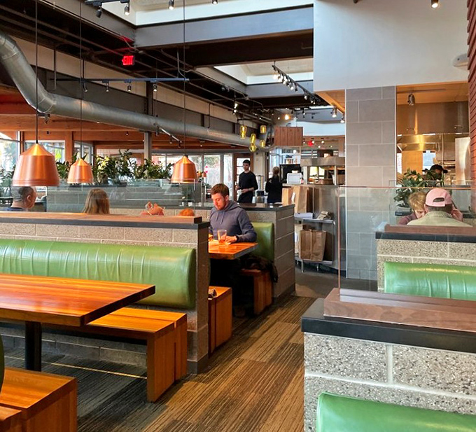Green booths and wooden tables create dining zones that feel private yet connected. The exposed ductwork says "industrial chic" without shouting it.