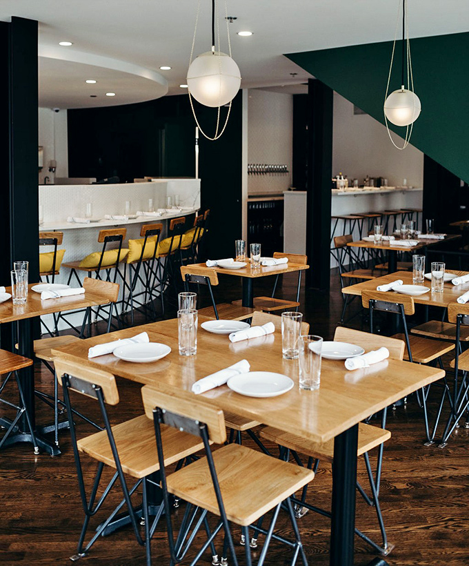 Clean lines, wooden chairs, and globe lighting create the perfect stage for the real star of the show: whatever's about to land on those white plates.