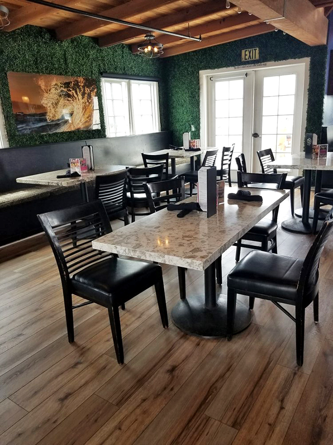 The artificial greenery wall adds a whimsical touch to this dining area, where marble-topped tables await seafood enthusiasts seeking harbor views.